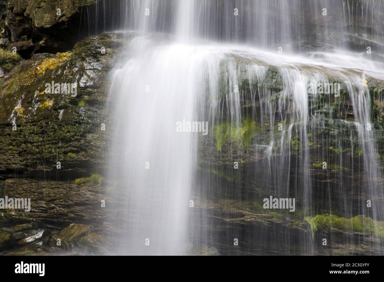 Waterfall surrounded by rocks covered in mosses under the sunlight ...
