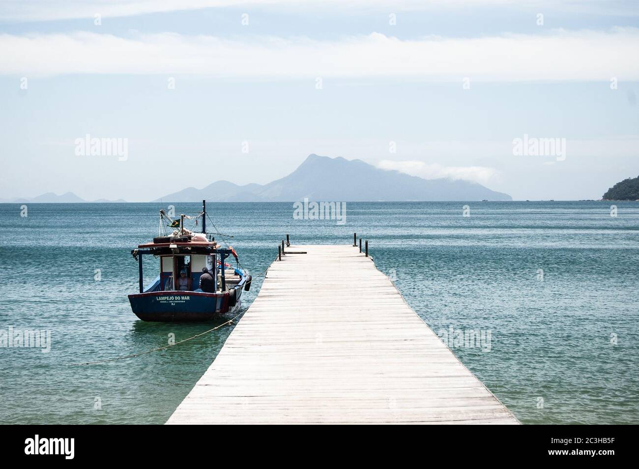 Wooden dock leading to the sea with a boat on the side in Ilha Grande ...