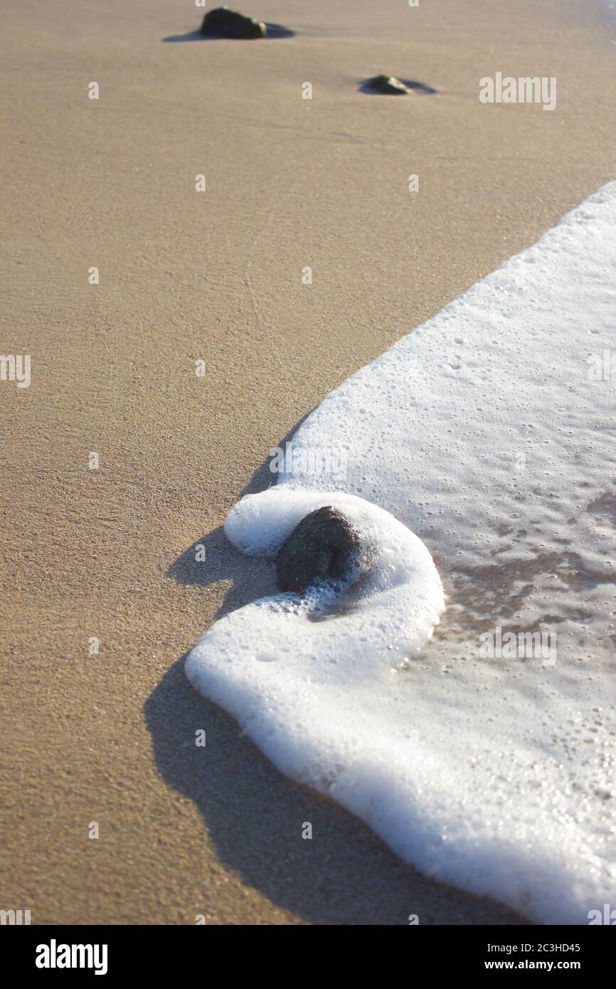 Stone in foam from a sea wave on the sand sunrise background of the sea ...