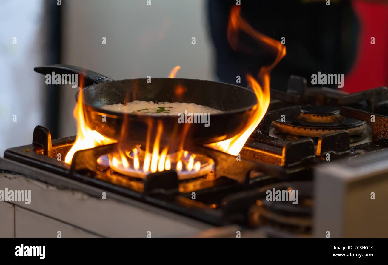 Pan of food sizzling on a gas hob over hot flames in a kitchen in a ...