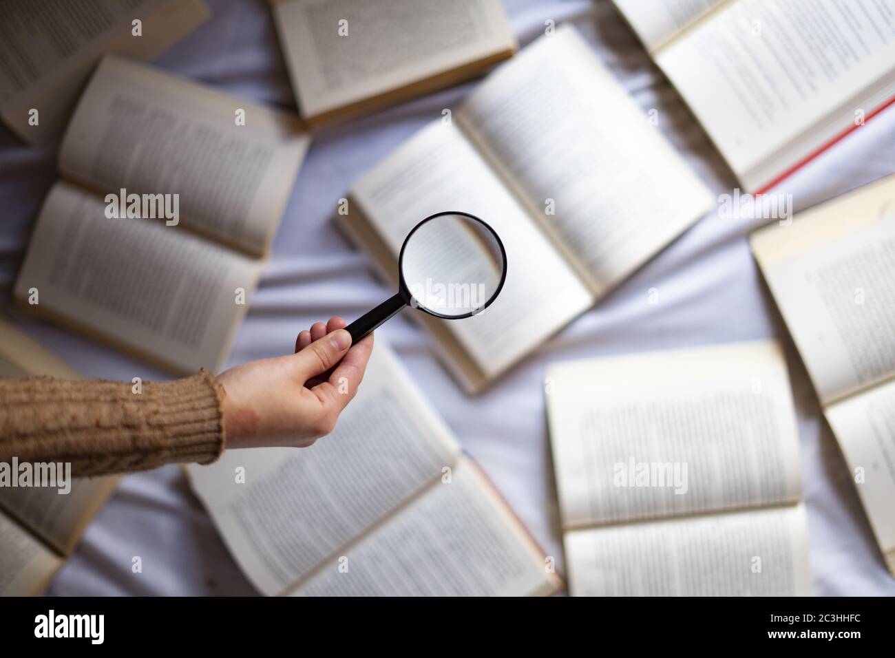 A top view of a cup of magnifier held in human hands on opened books ...