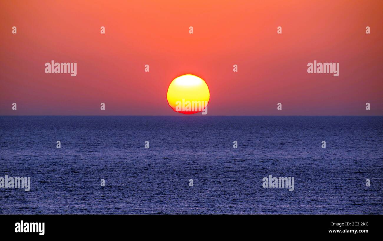 Wonderful summer sunset over the blue sea with a large sun illuminating ...