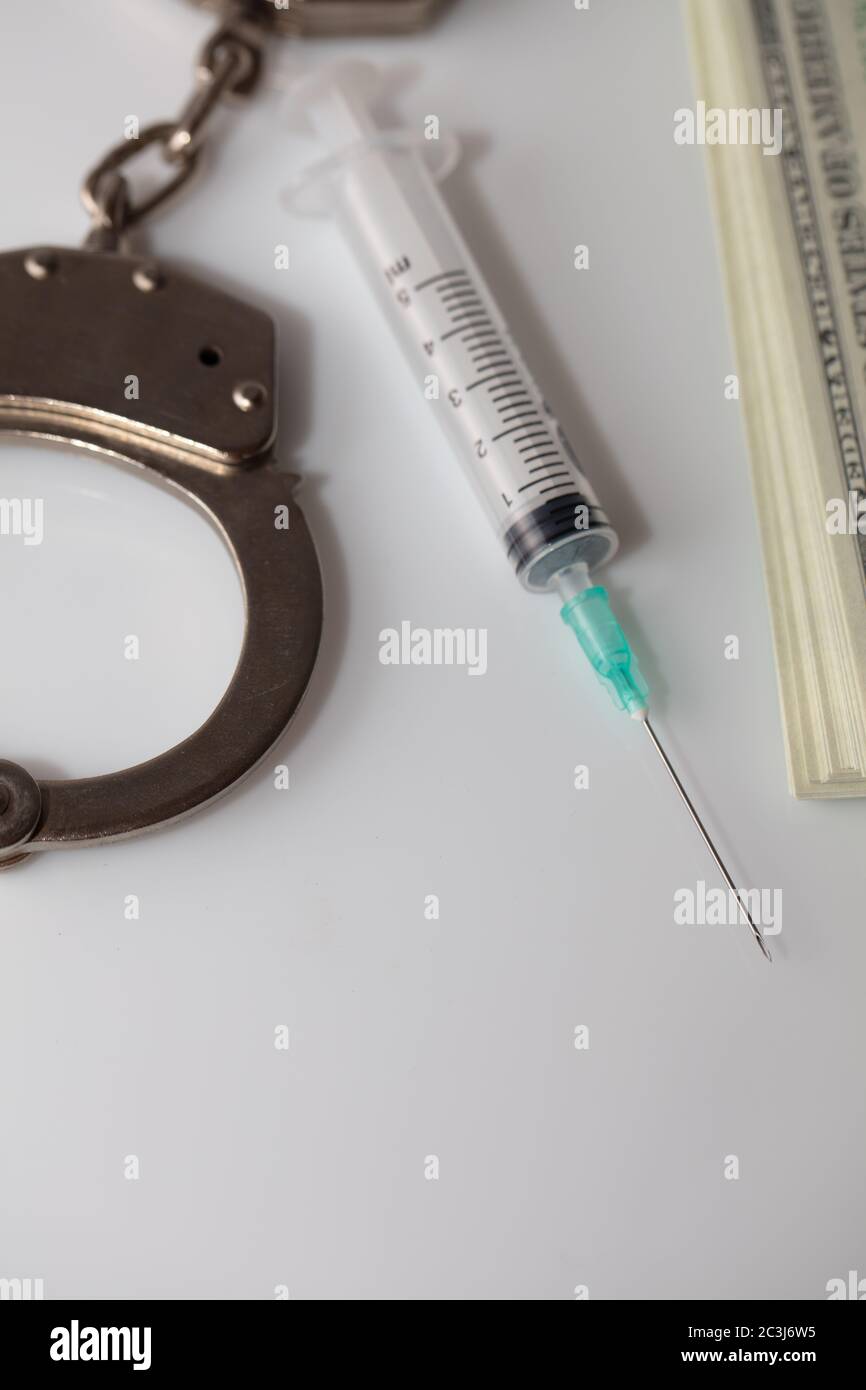 Vertical high angle shot of handcuffs, a syringe, and some dollar bills ...