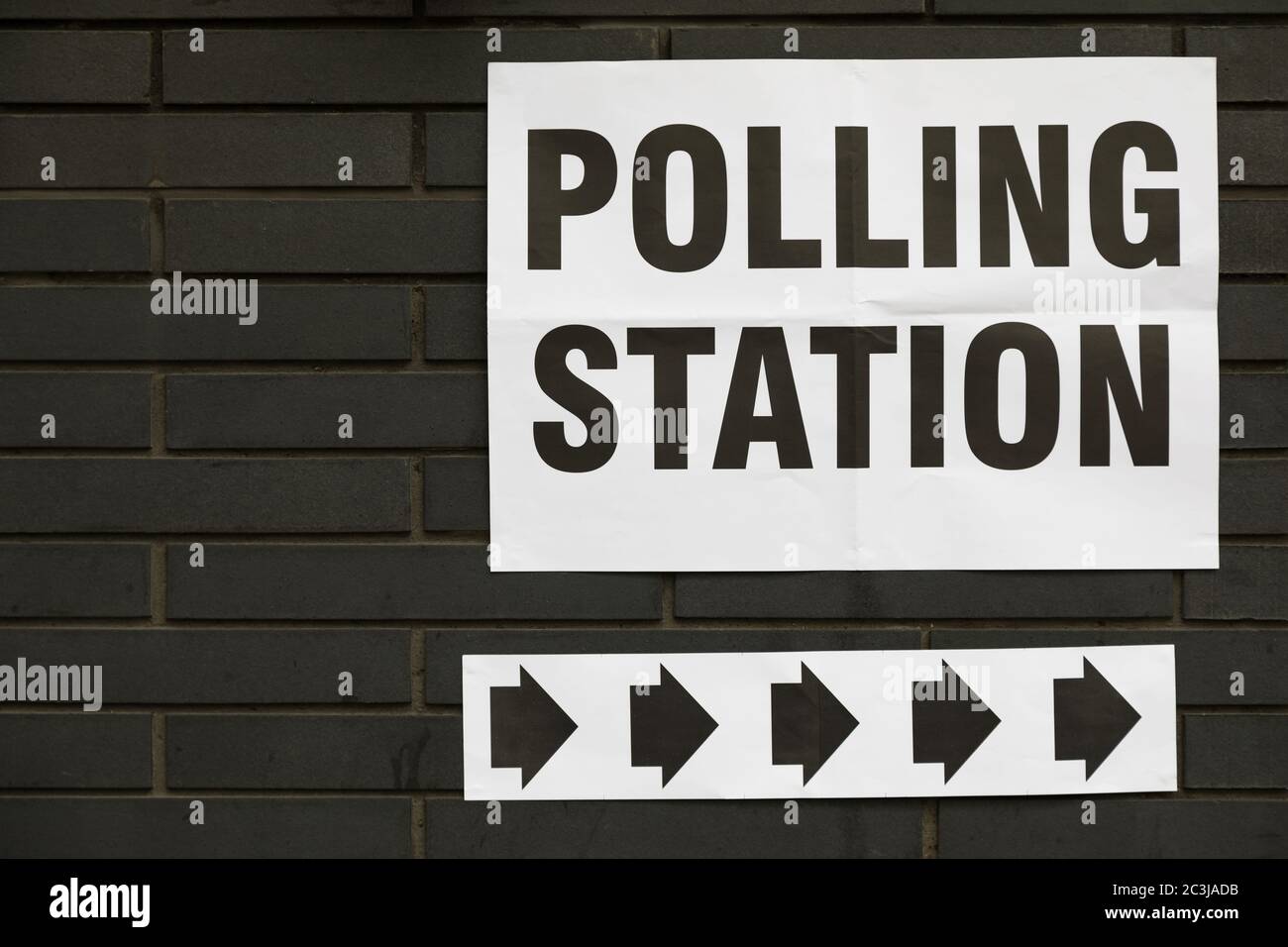 Polling Station sign on black brick wall in London, UK, with arrows ...