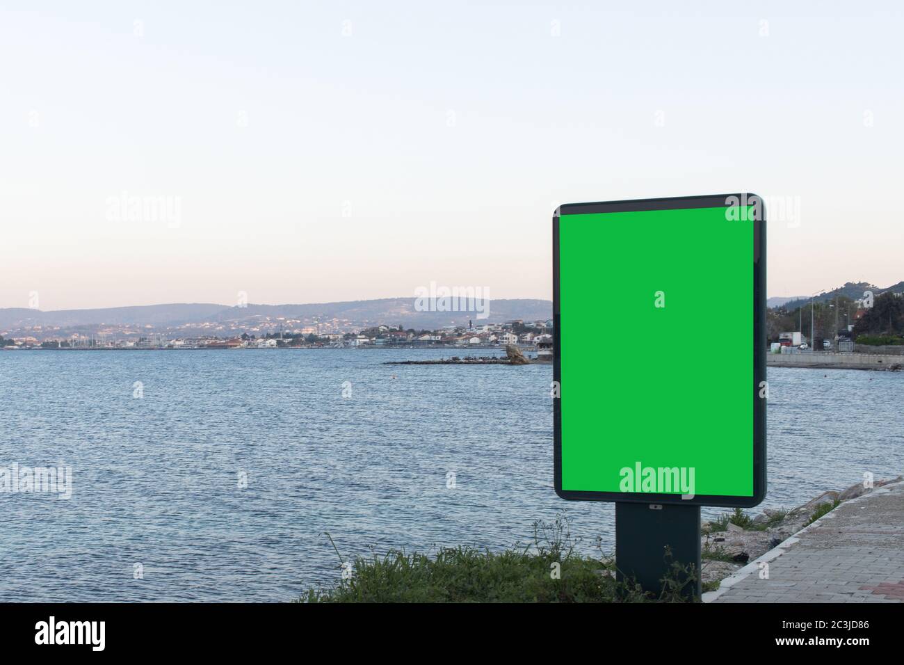 Big green sign by the lake under the bright sky with a city in the ...