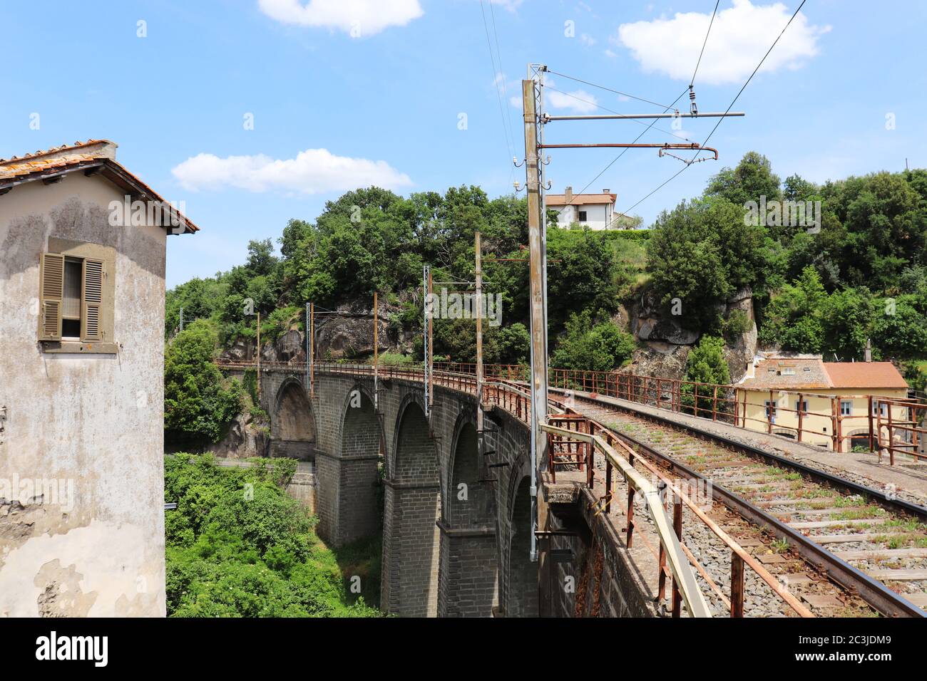 The railroad tracks pass over a stone bridge through a landscape full ...