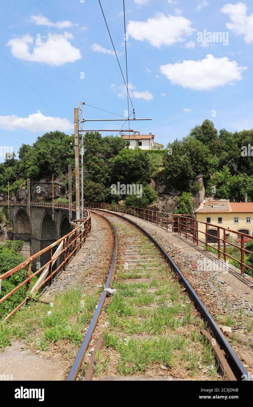 The railroad tracks pass over a stone bridge through a landscape full ...
