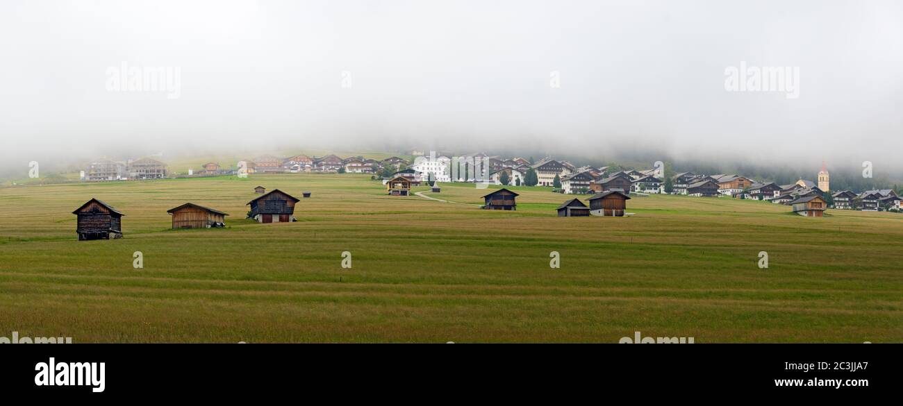 meadow slope with hay barns below the village of Obertilliach at foggy ...