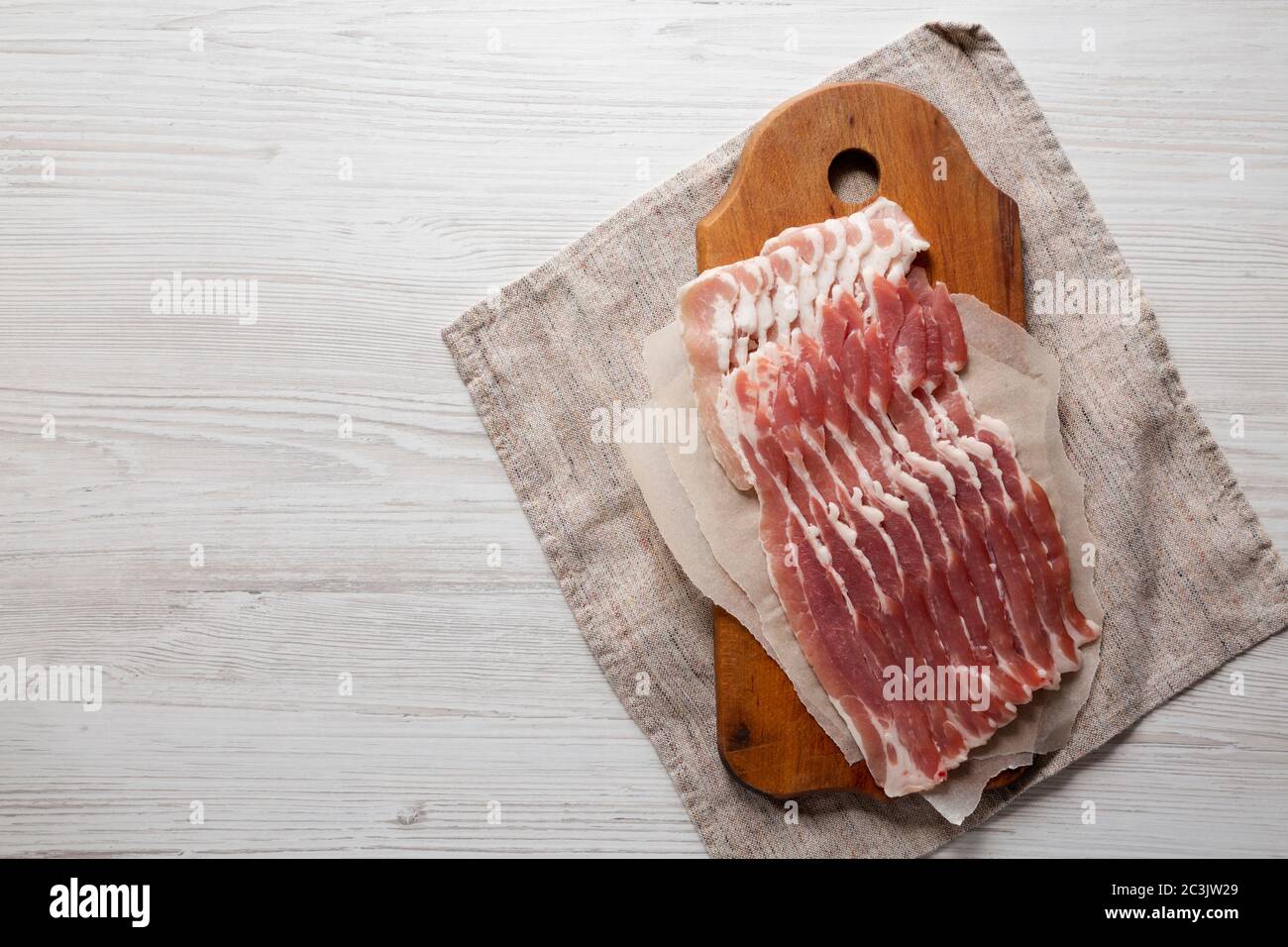Uncooked Raw Bacon on a rustic wooden board on a white wooden ...