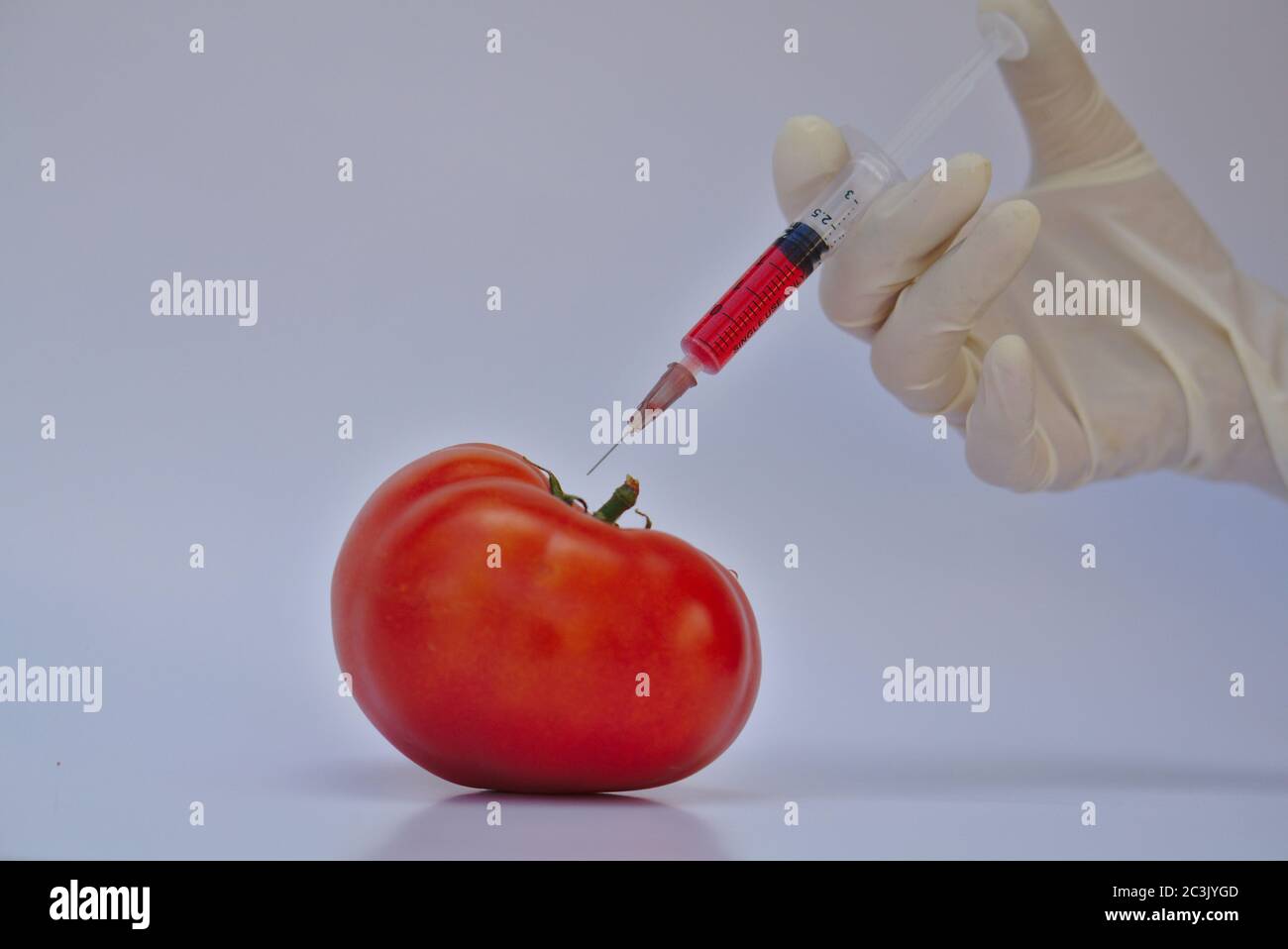 Hand with syringe injecting a tomato against a white background. A GMO ...