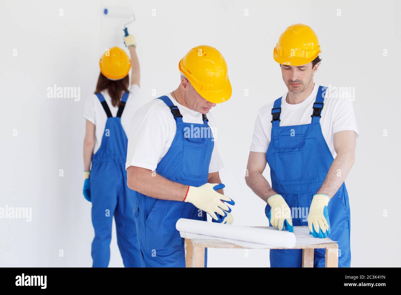 Workers in blue uniform and yellow hardhats with blueprint working at ...