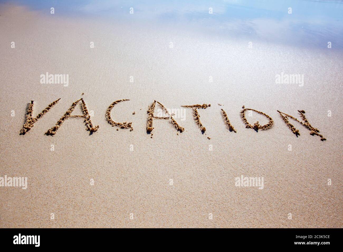 Word vacation written in a sandy tropical beach with soft sea wave ...