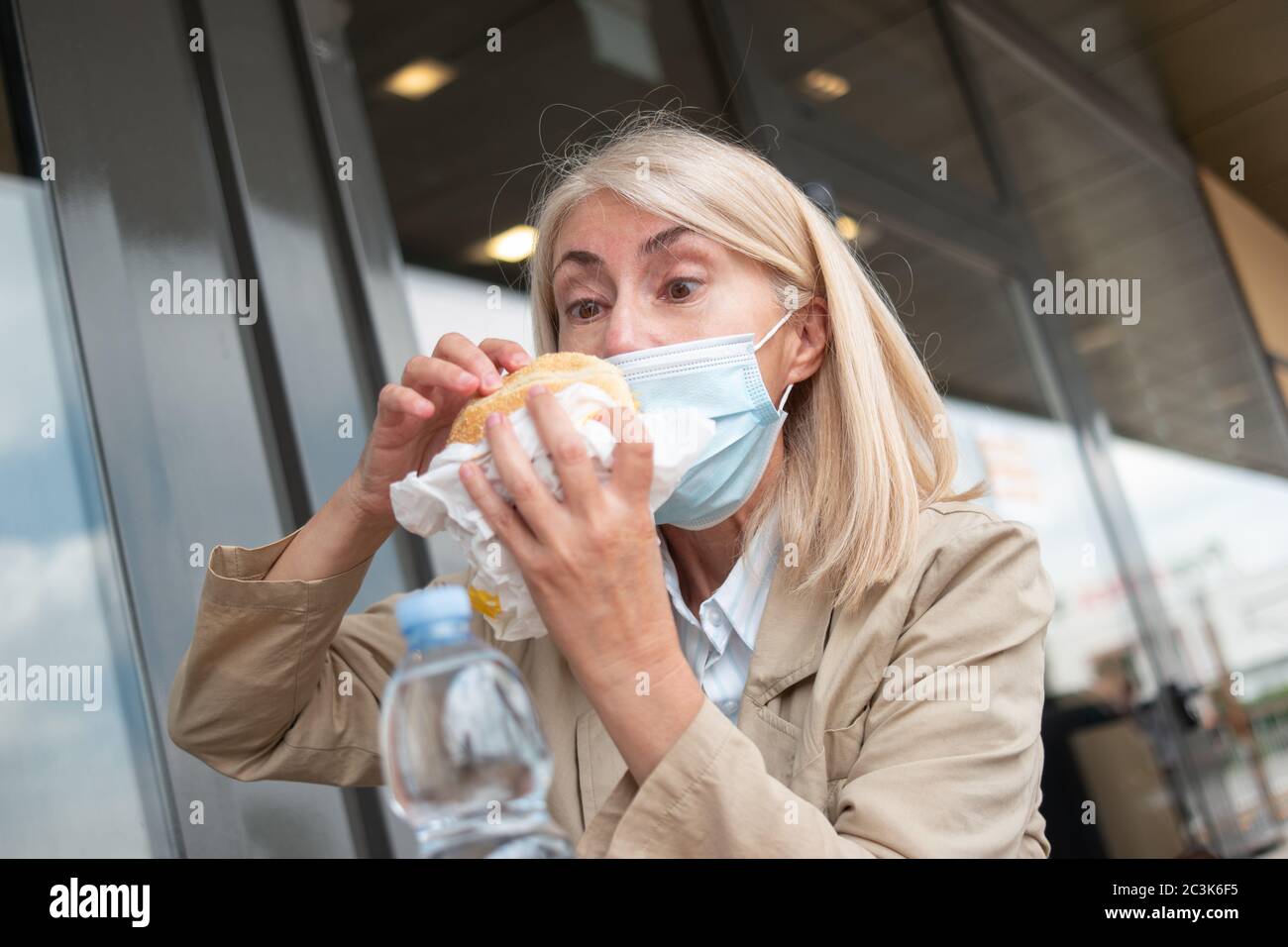 Woman trying to eat his fast food lunch hamburger while wearing a mask ...