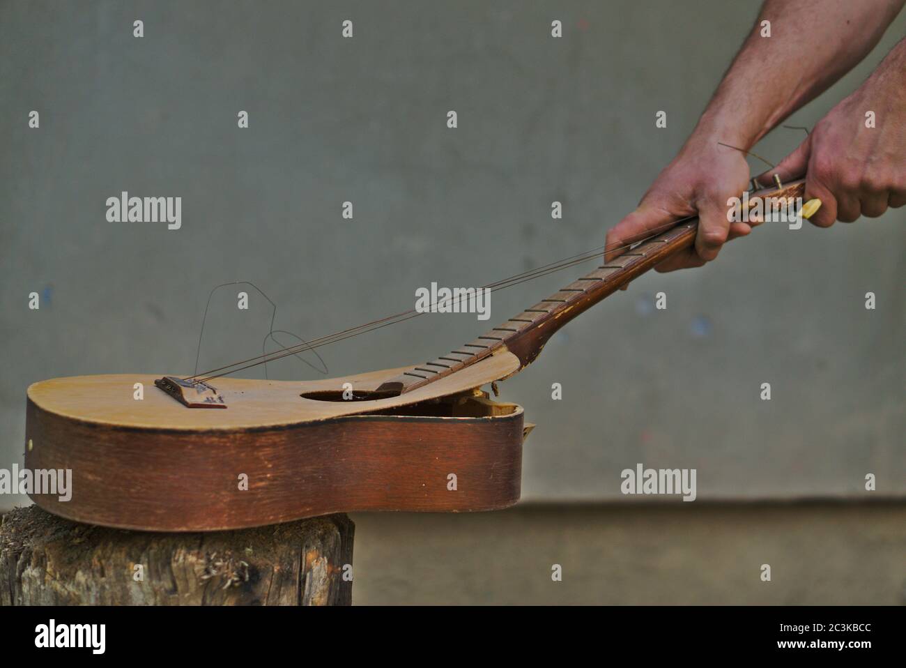 Angry male breaking the guitar by hitting it on a log with a blurred ...