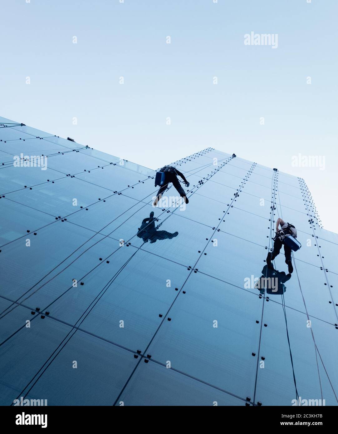 Low angle shot of two persons rappelling at the side of a tall building ...
