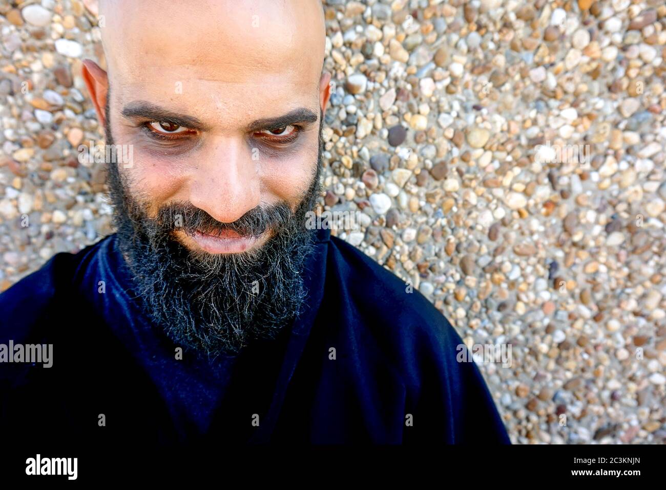 Closeup shot of a bald bearded man smiling with a stone wall on the ...