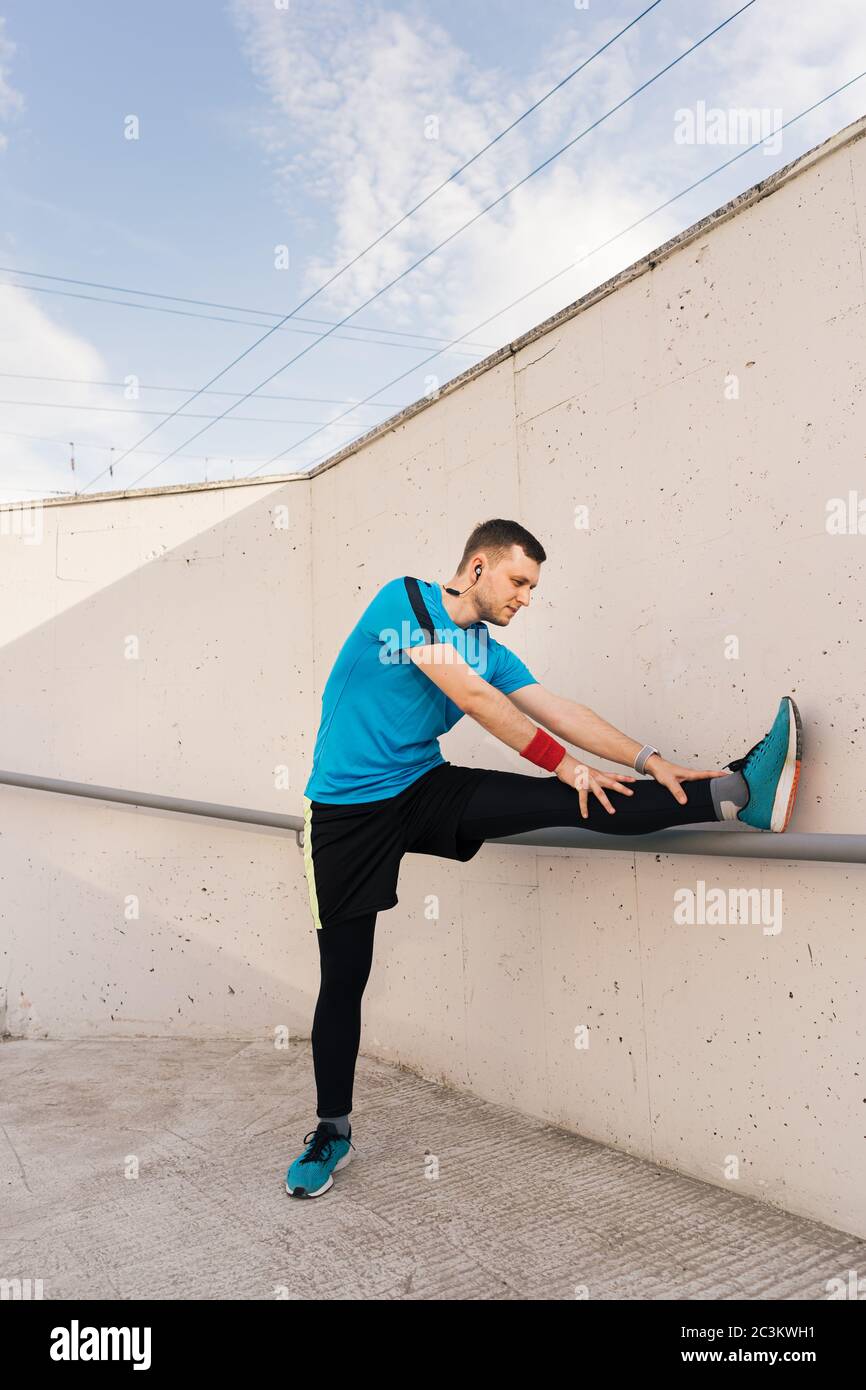 Young man runner getting ready to run stretching legs warm up quad ...