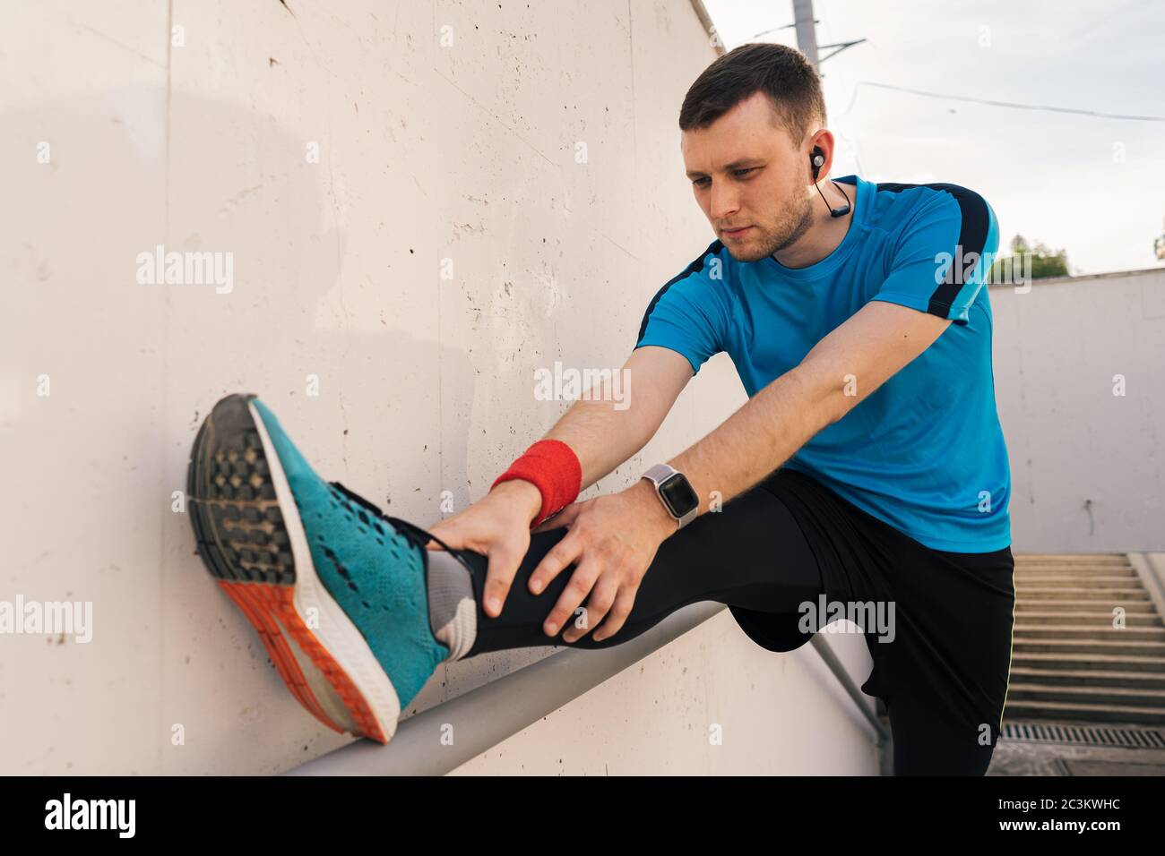 Young man runner getting ready to run stretching legs warm up quad ...