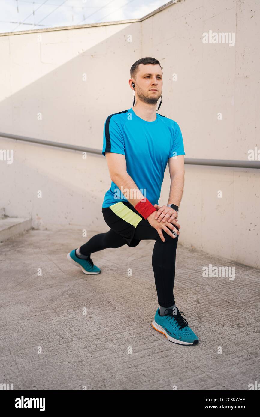 Young man runner getting ready to run stretching legs warm up quad ...