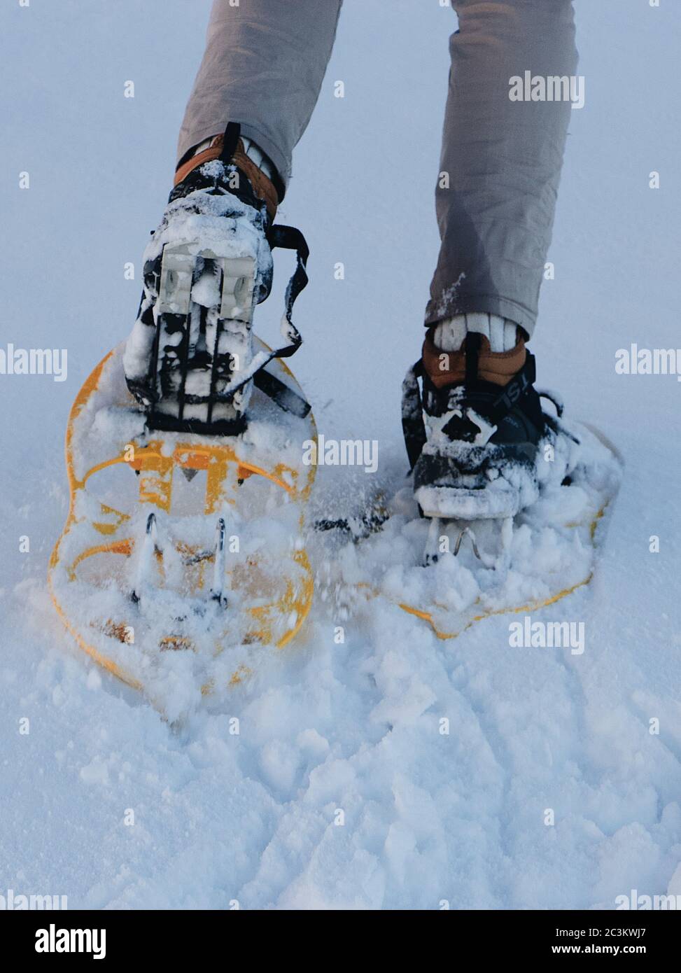 Vertical shot of feet wearing snowshoes on the mountains covered with ...