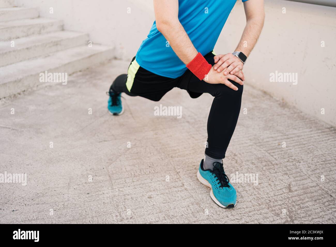 Young man runner getting ready to run stretching legs warm up quad ...