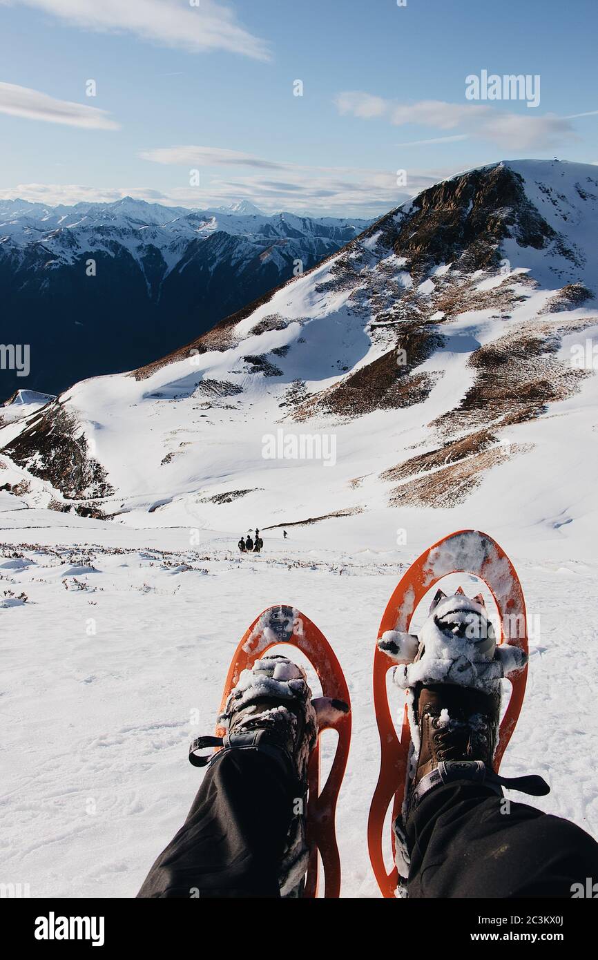 Vertical shot of feet wearing snowshoes on the mountains covered with ...