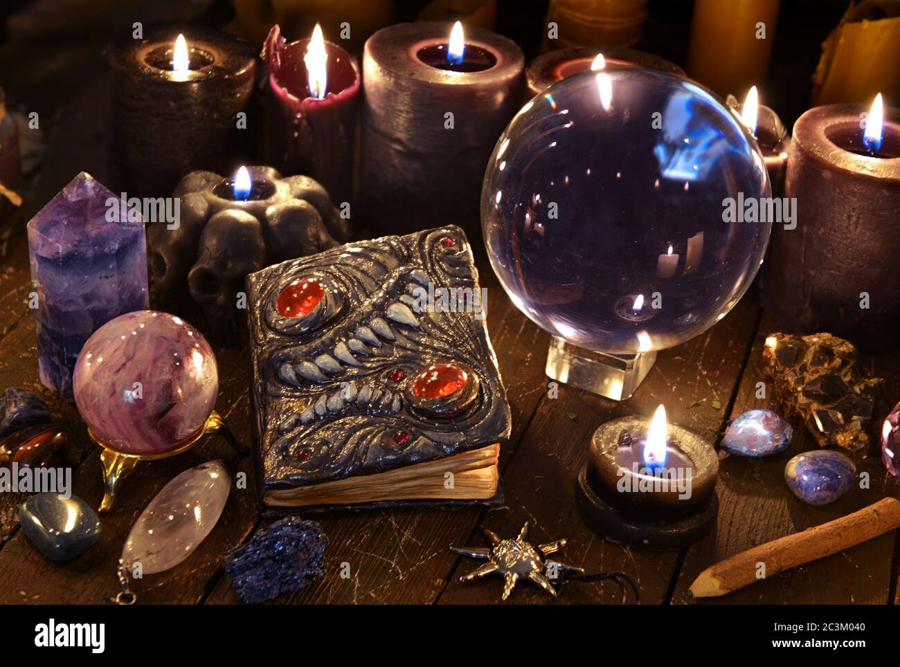 Crystal ball, magic book and burning black candles on witch table ...