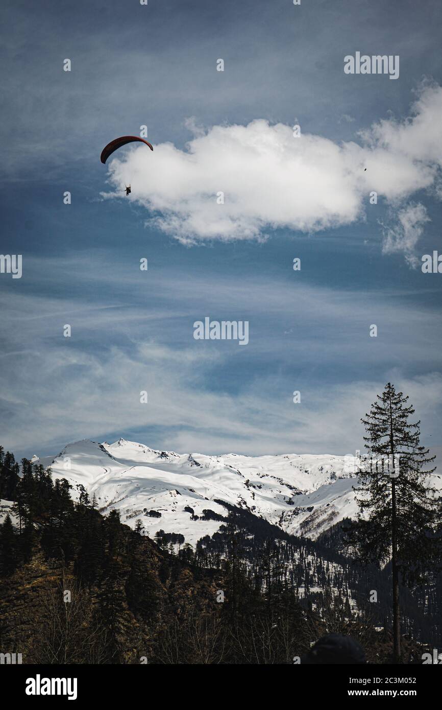 Vertical shot of a person paragliding in the snow-covered mountains in ...