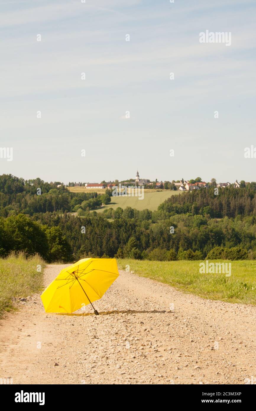 Vertical shot of an open yellow umbrella on the road in the countryside ...