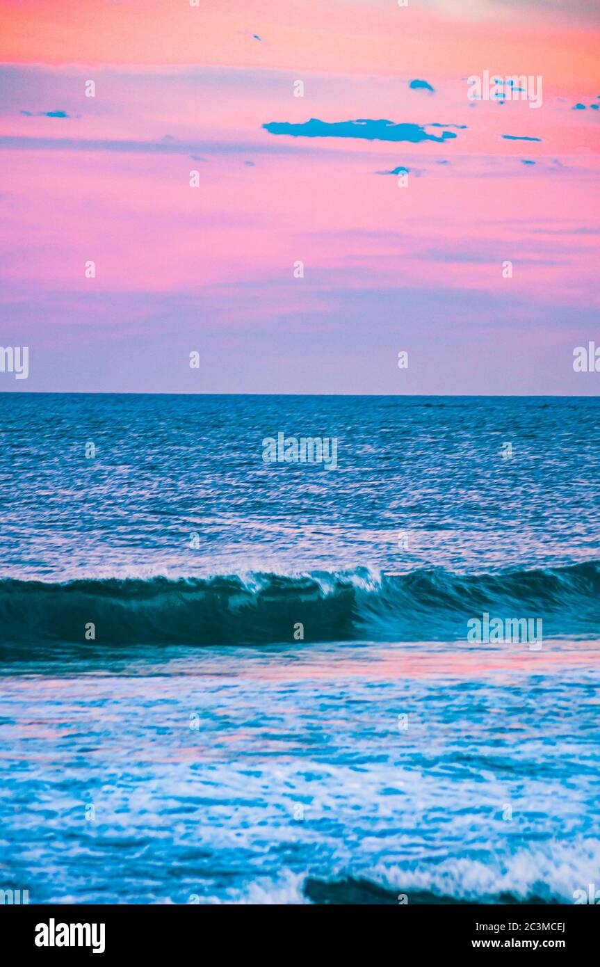 Mesmerizing shot of the waves of the ocean glimmering under the pink ...