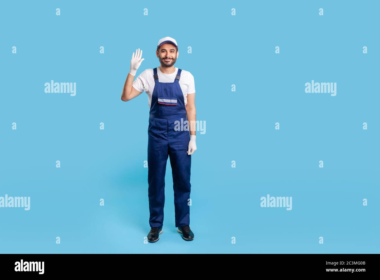 Full length friendly handyman in overalls and protective gloves ...
