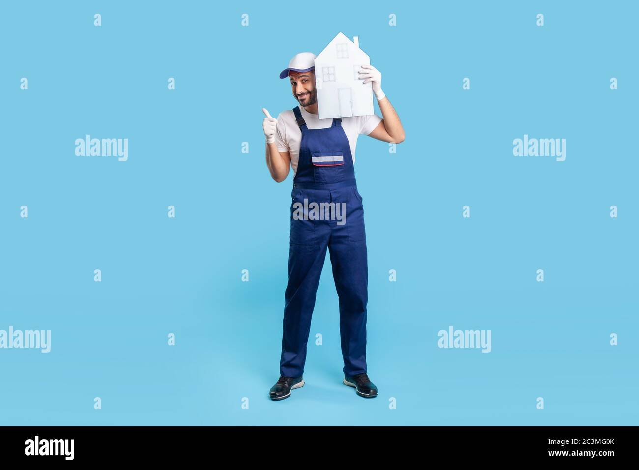 Full length happy labourer in uniform holding paper house on shoulder ...