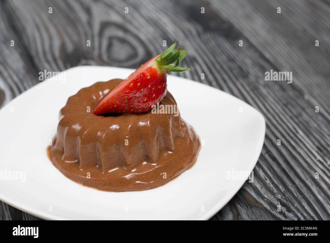 Chocolate fudge garnished with half a strawberry with petals. Saucer ...