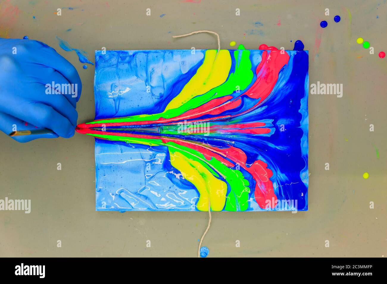 Hand pulling string lines through rows of coloured acrylic paint on an ...