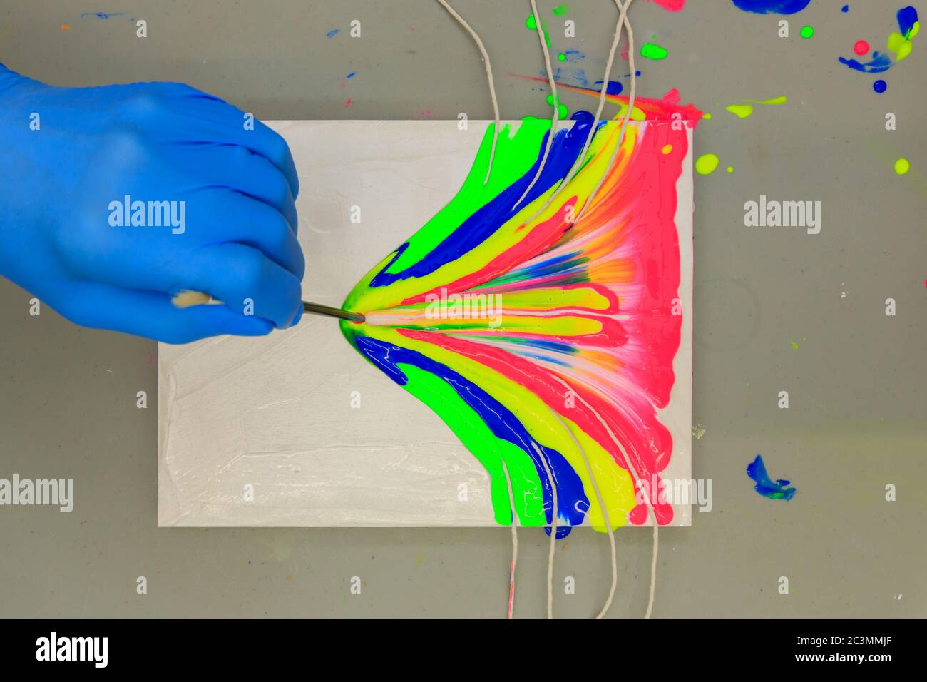 Hand pulling string lines through rows of coloured acrylic paint on an ...