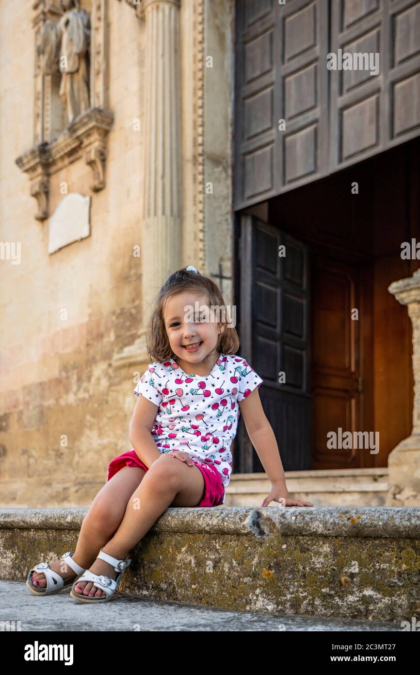 A beautiful and smiling little girl, sitting on the steps of the ...