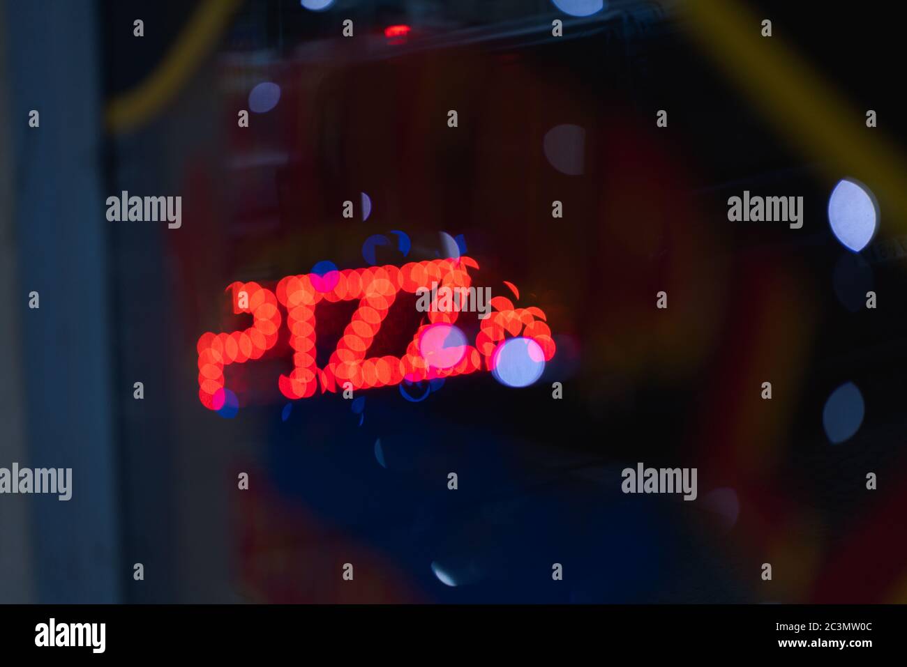 Closeup of a glowing red pizza sign through a glass window with bokeh ...