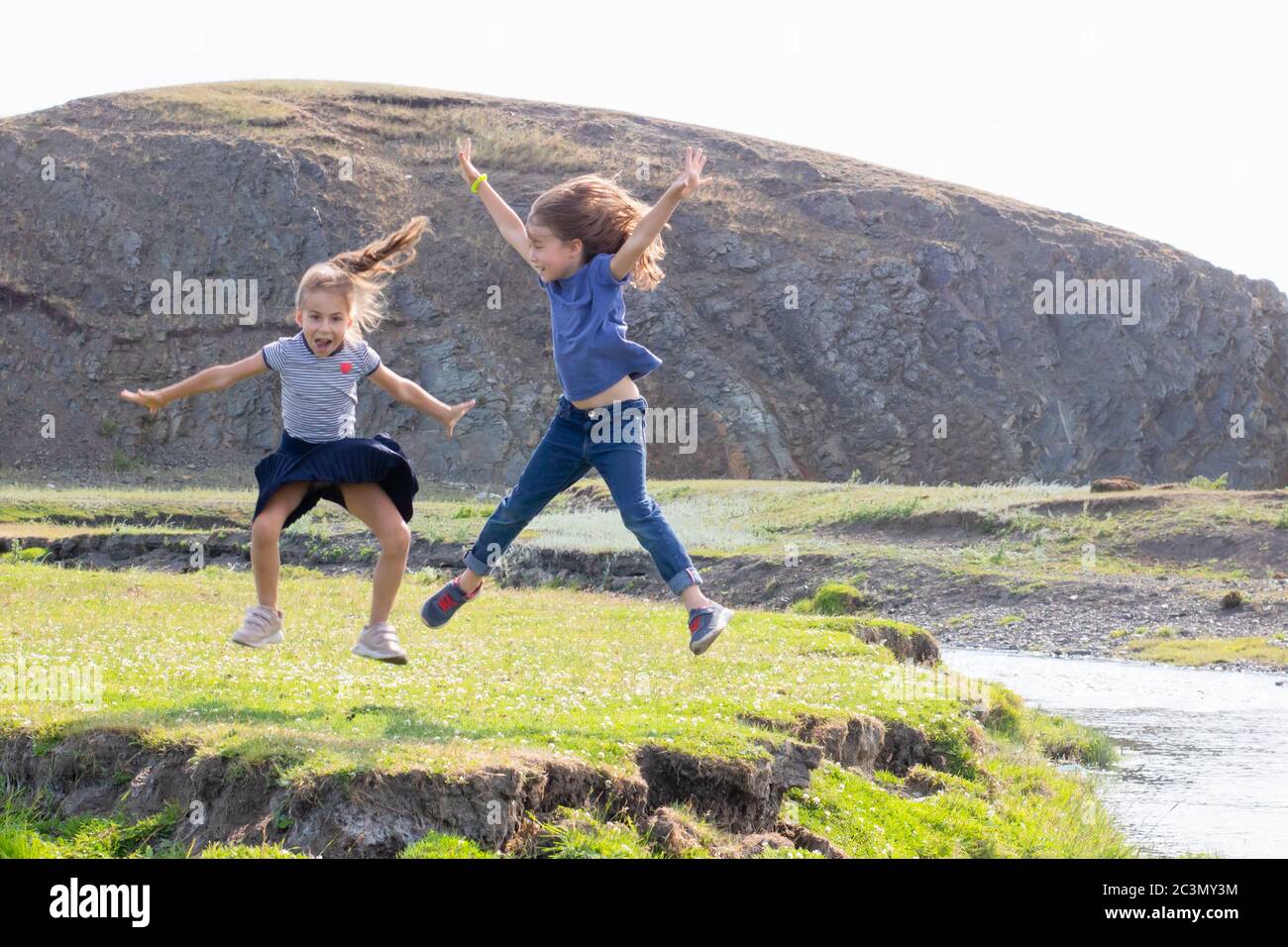Cheerful children are jumping in the summer on the lawn by the river ...