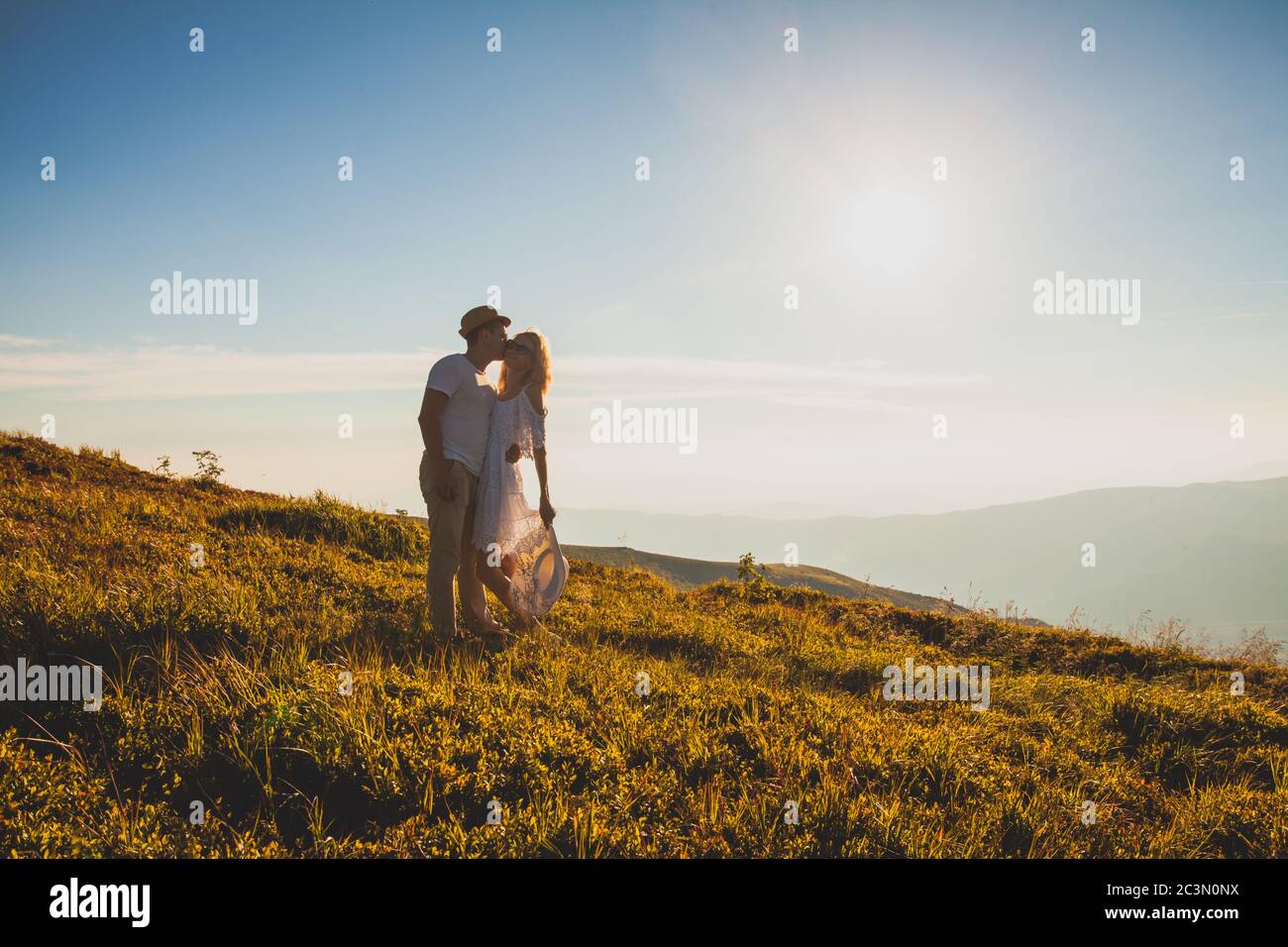 Embracing romantic couple in white on a hill Stock Photo - Alamy