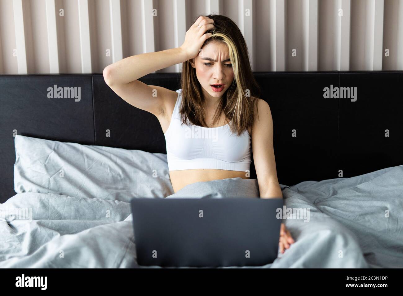 Young woman looking in laptop screen and holding her head in confusion ...