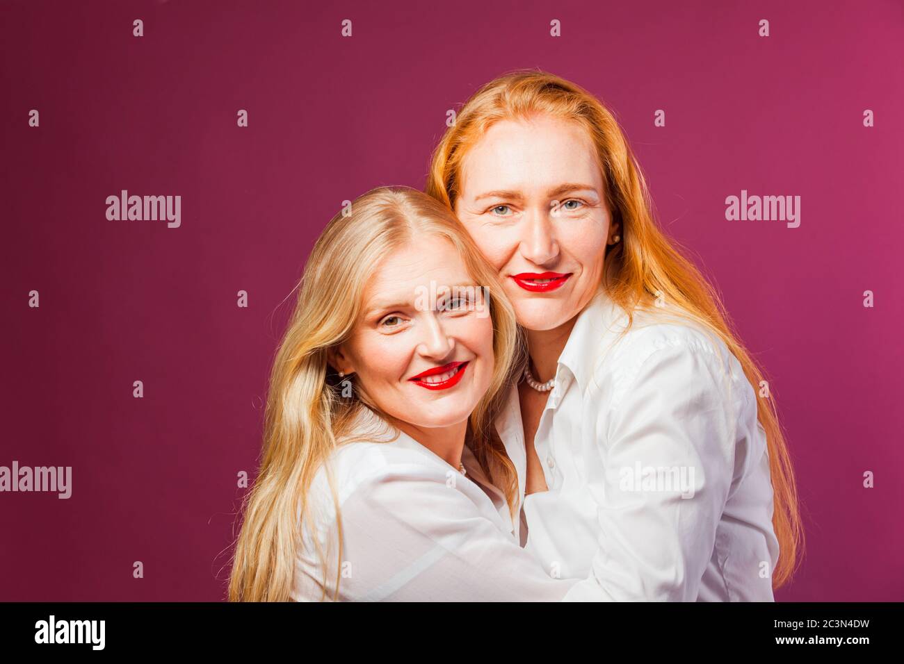 Two pretty sisters hugging on purple background Stock Photo - Alamy