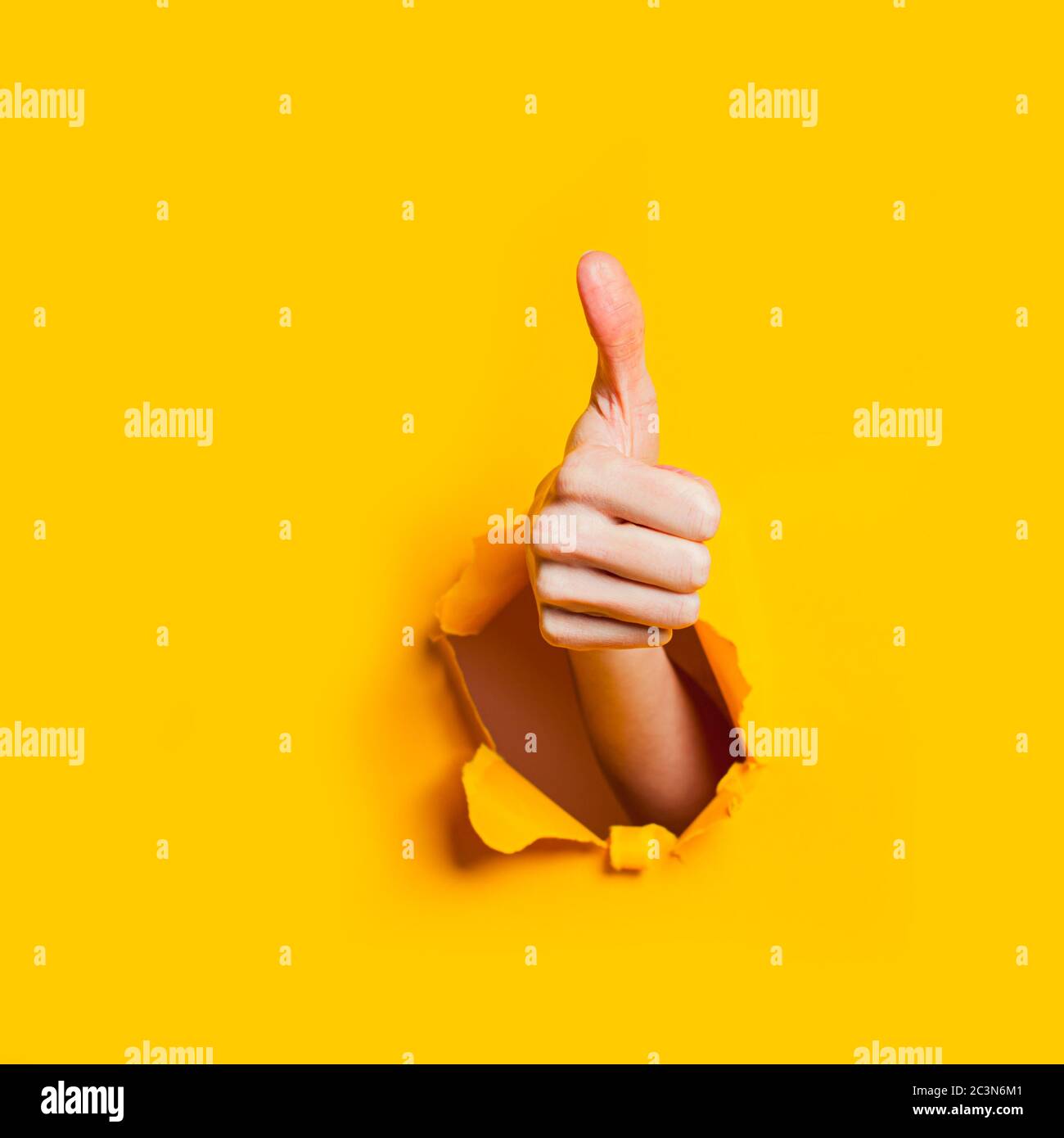 Hand showing a thumb up sign through a ripped hole in yellow paper ...