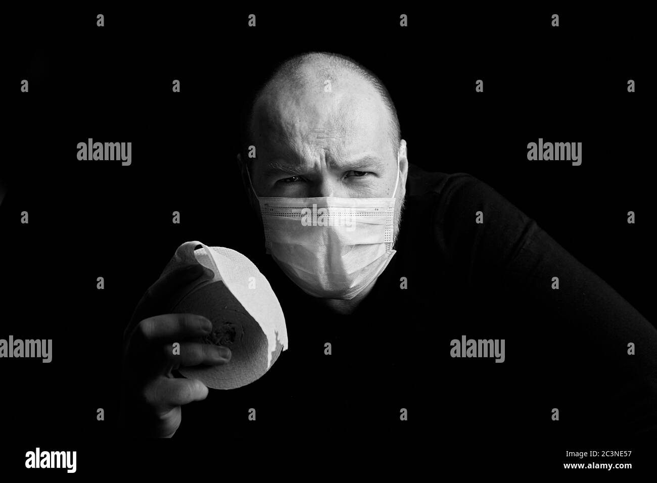 Man in a face mask holding toilet paper roll on black background ...