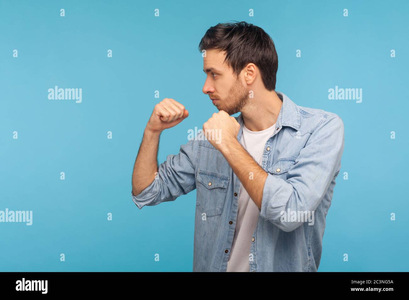 Side view of man in worker denim shirt standing with boxing gesture ...