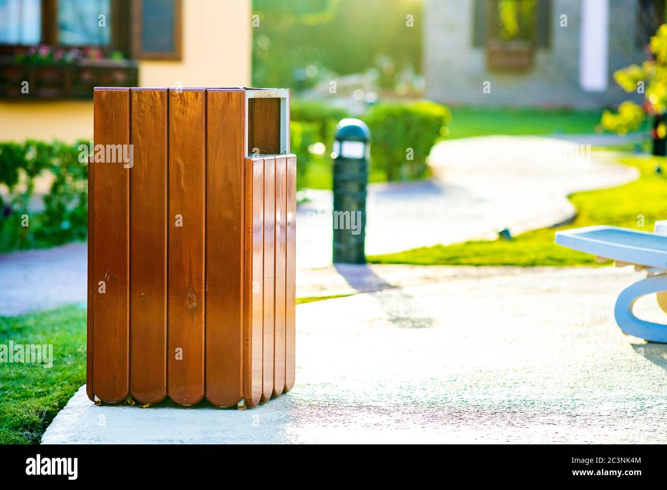 Yellow wooden trash can outdoors on the side of sidewalk in park ...