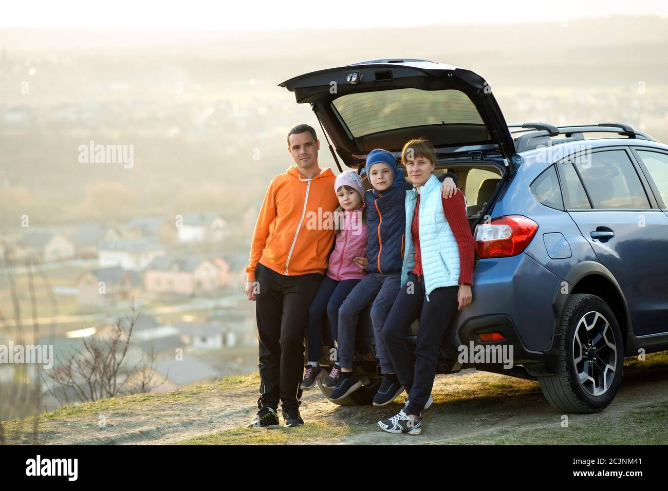 Happy family standing together near a car with open trunk enjoying view ...