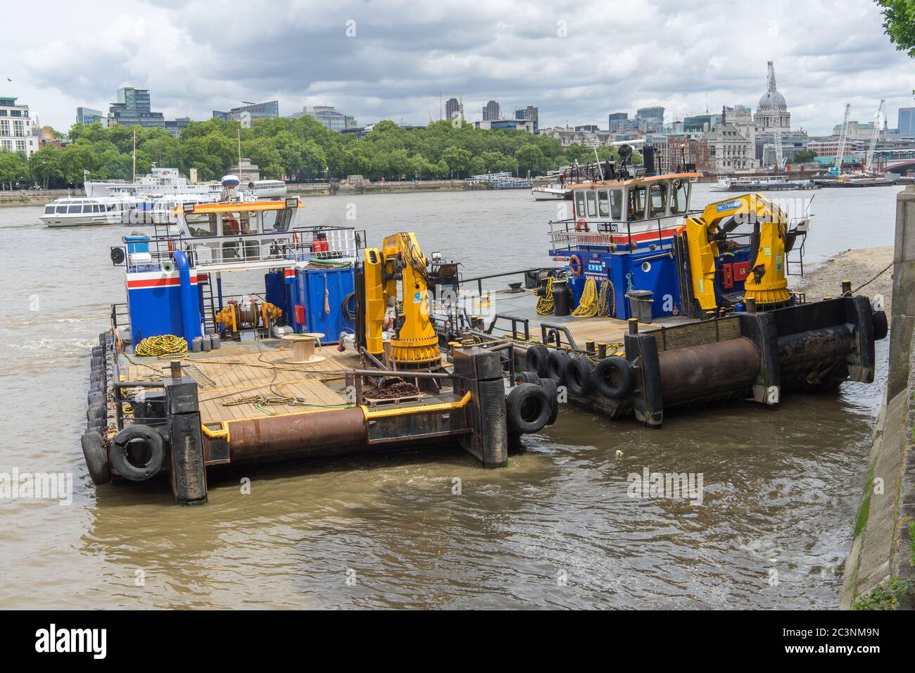 Floating barges along the River Thames with small yellow construction ...