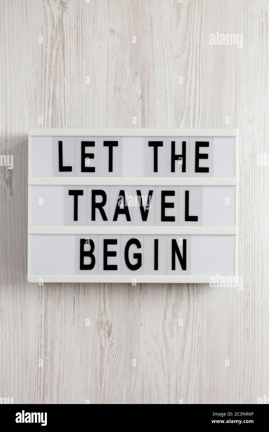 'Let the travel begin' on a lightbox on a white wooden background, top ...