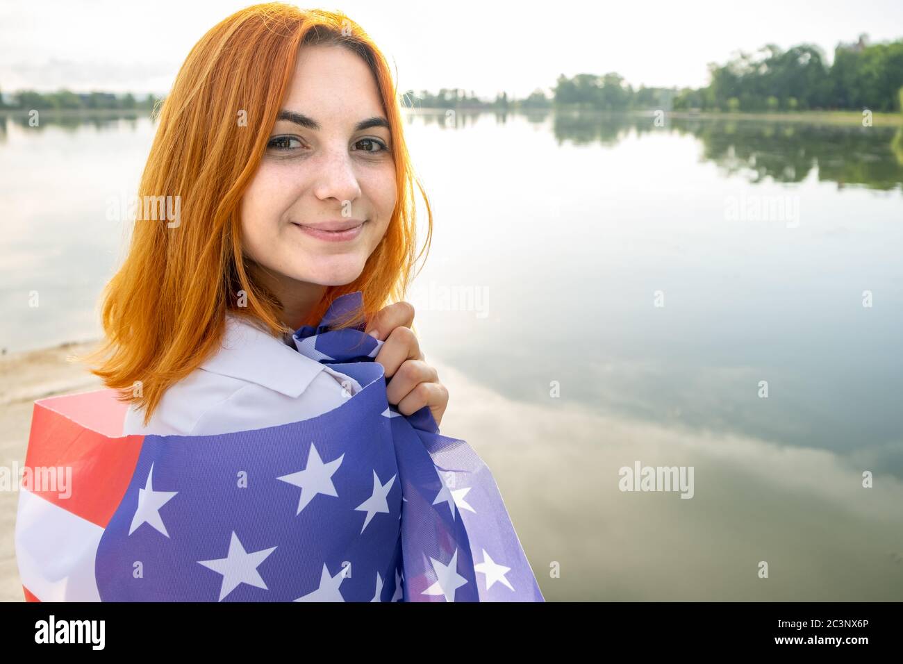 Portrait of happy smiling girl with USA national flag on her shoulders ...