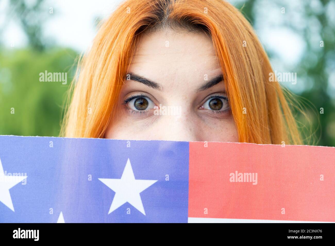 Portrait of happy smiling red haired girl hiding her face behind USA ...